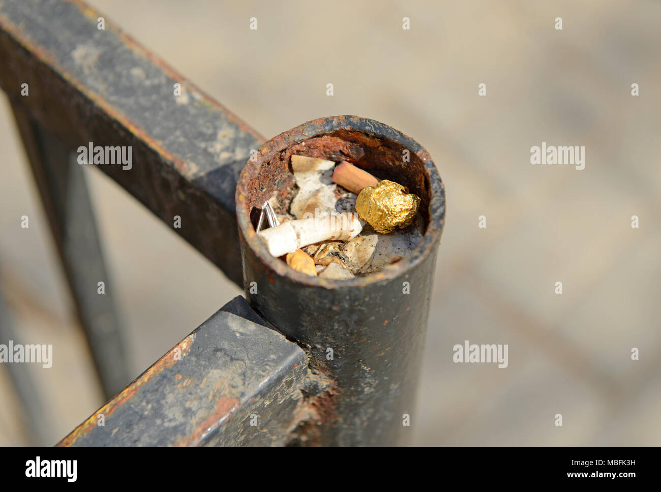 Discarded cigarette stubs and rubbish in the well of a fence upright in ...