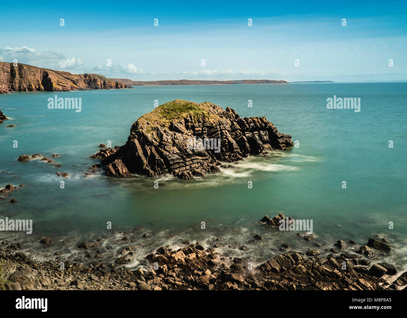 Seaside rock away from the shore. With green blue ocean water and blue ...