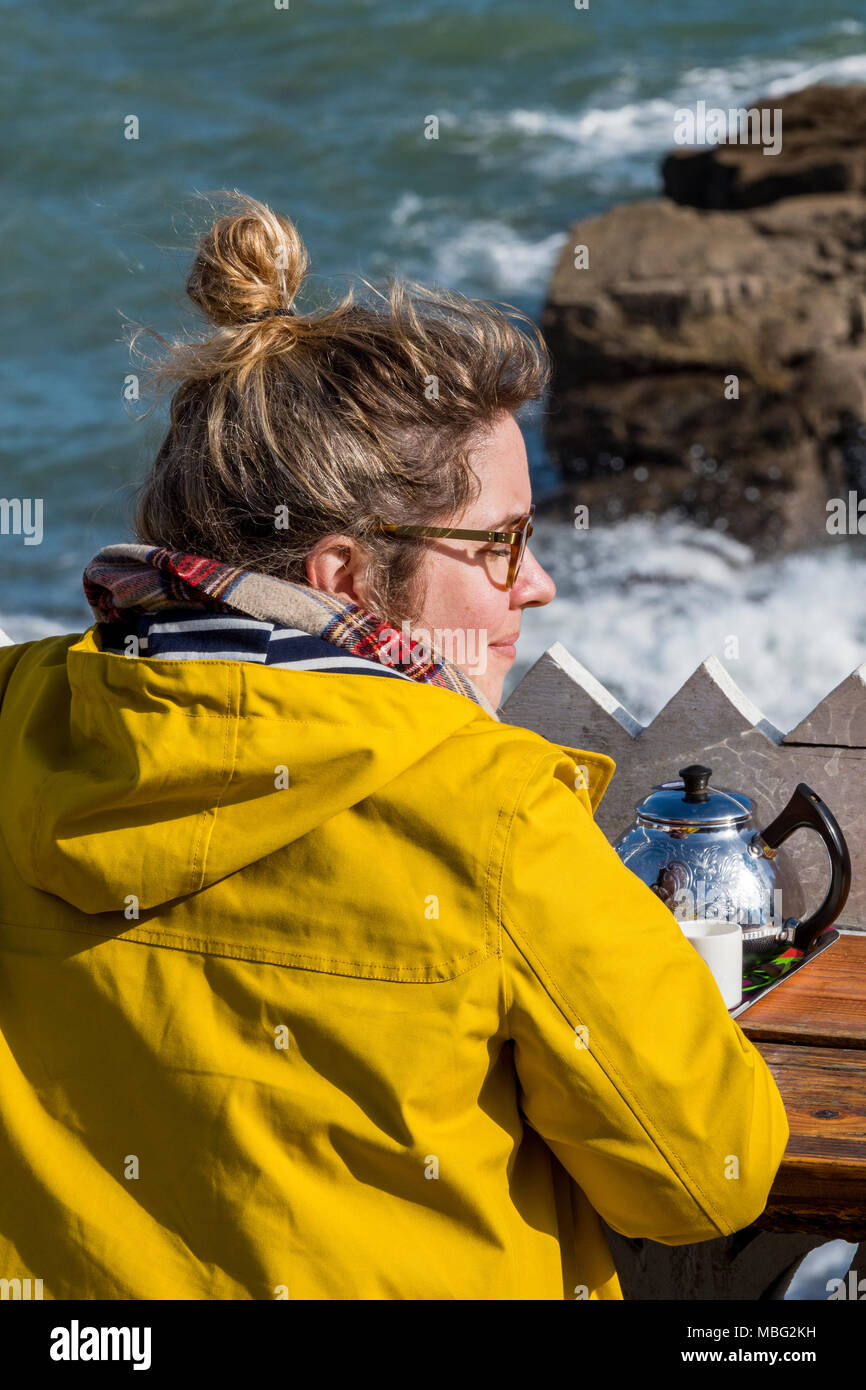 A woman or female sitting drinking tea with a yellow coast and teapot ...