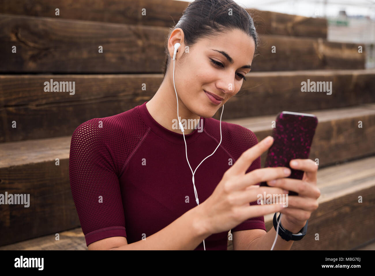 Pretty woman looking at phone and smiling in maroon shirt and white ear ...