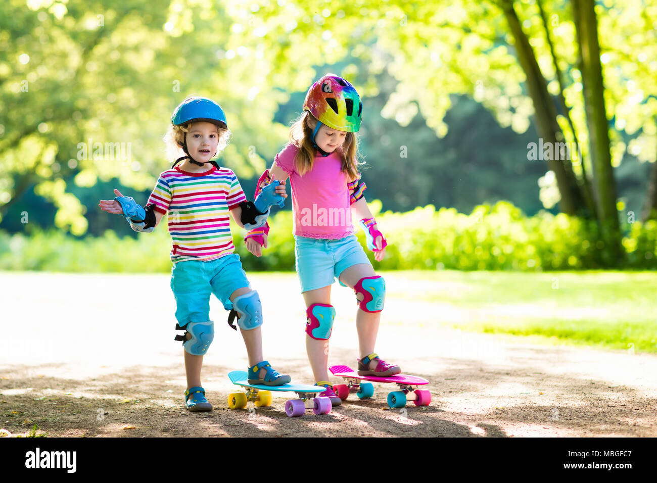 Children riding skateboard in summer park. Little girl and boy learn to ...