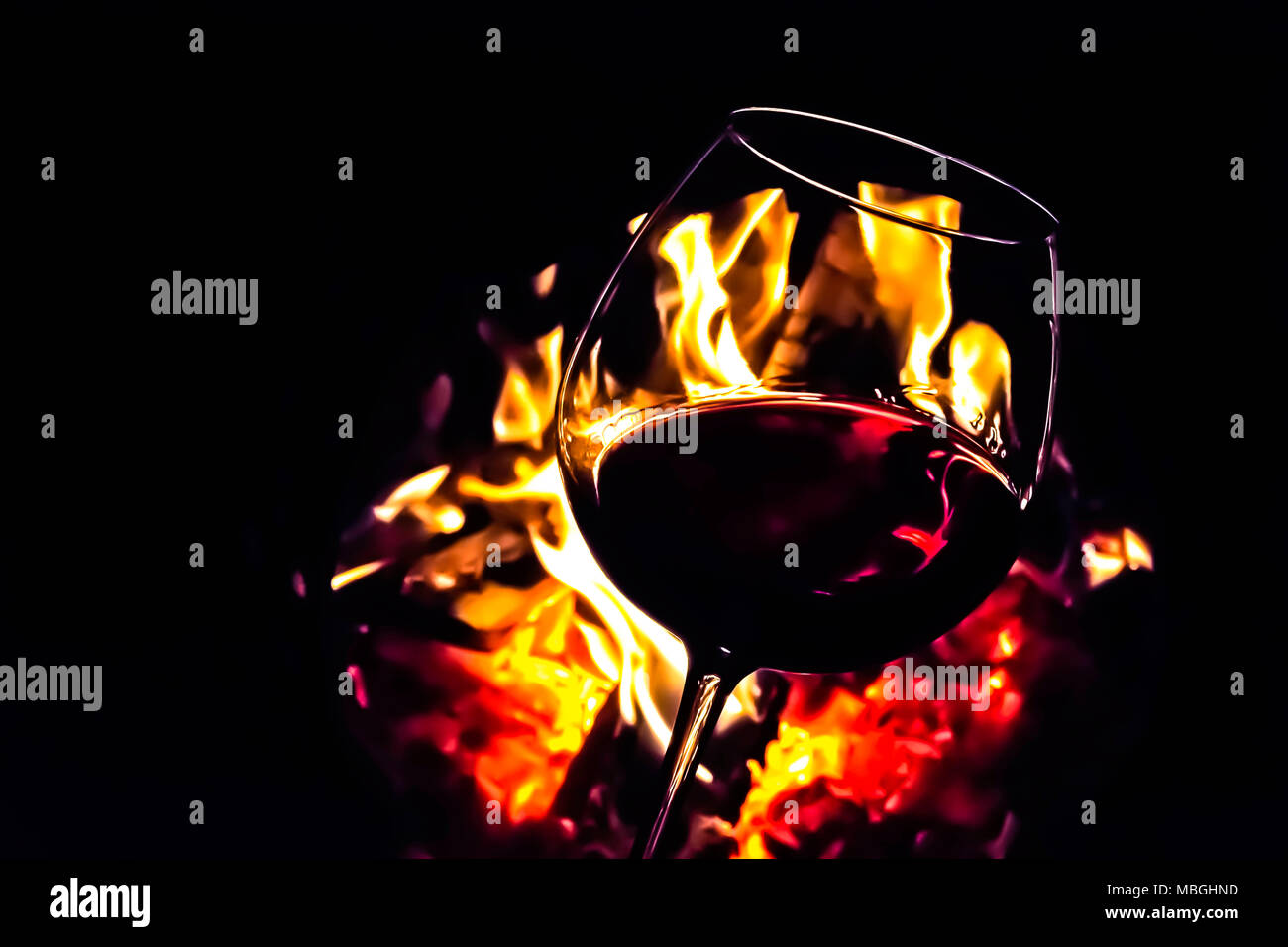Glass of red wine backlighted by campfire flames.Moody dark atmosphere ...