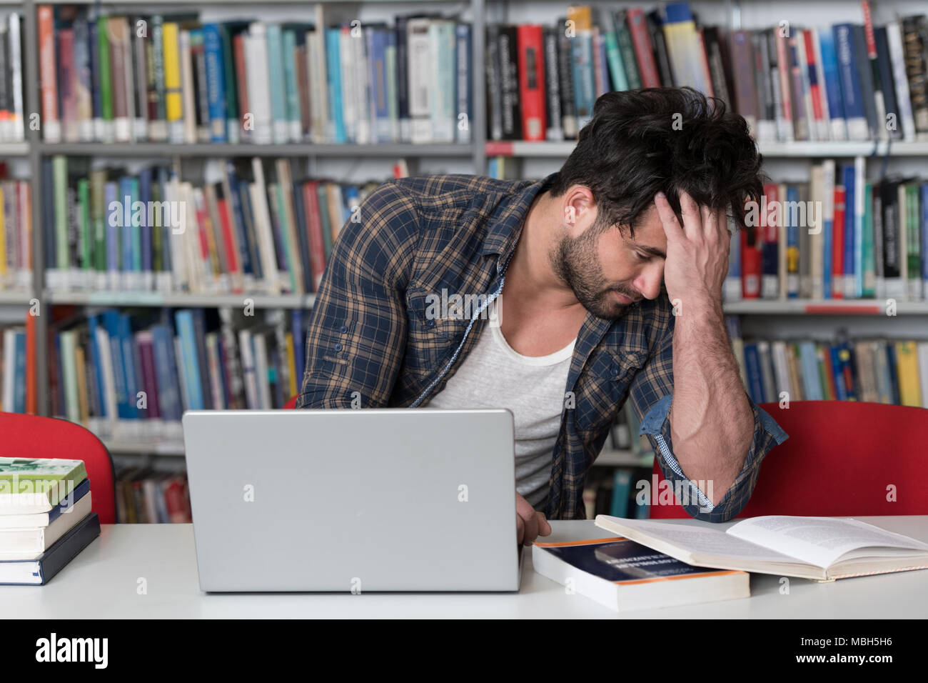 Stressed Young Male Student Reading Textbook While Sitting in Library ...