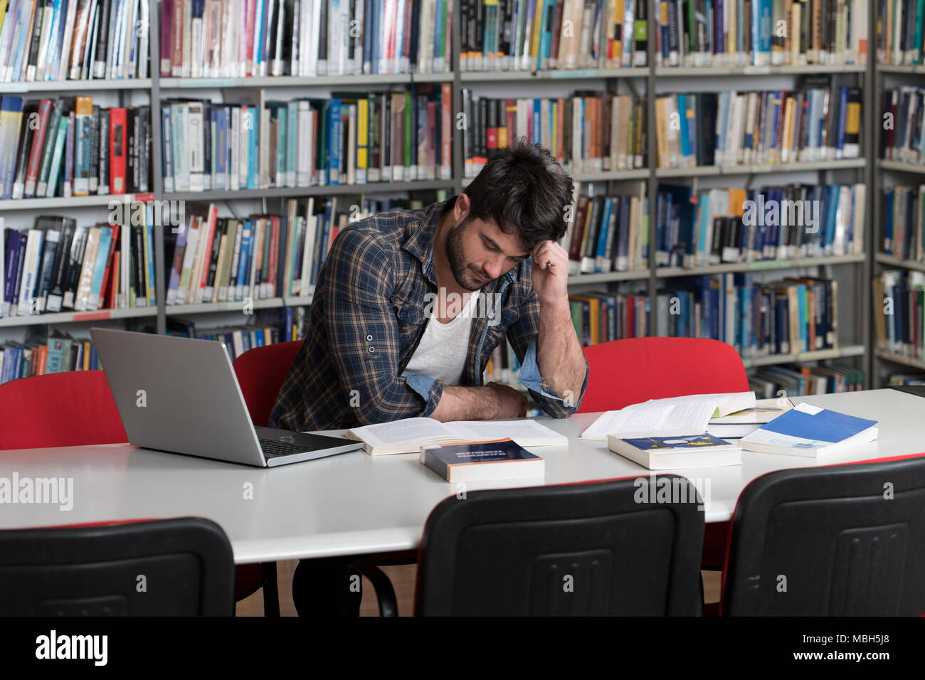 Stressed Young Male Student Reading Textbook While Sitting in Library ...