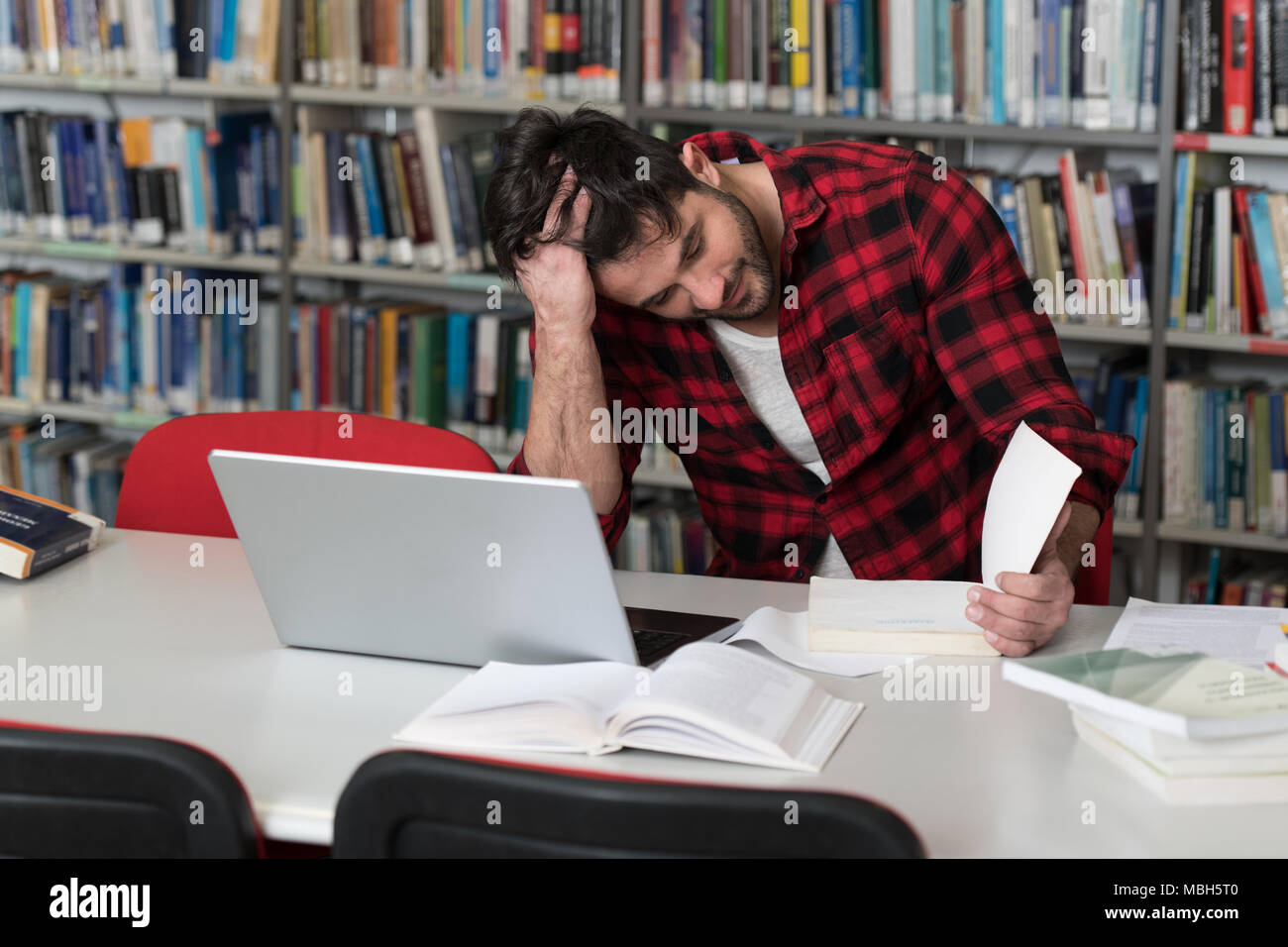 Stressed Young Male Student Reading Textbook While Sitting in Library ...