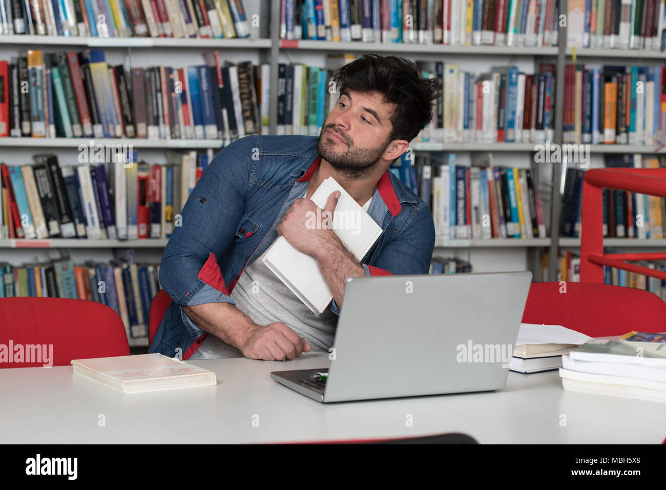 Stressed Young Male Student Reading Textbook While Sitting in Library ...