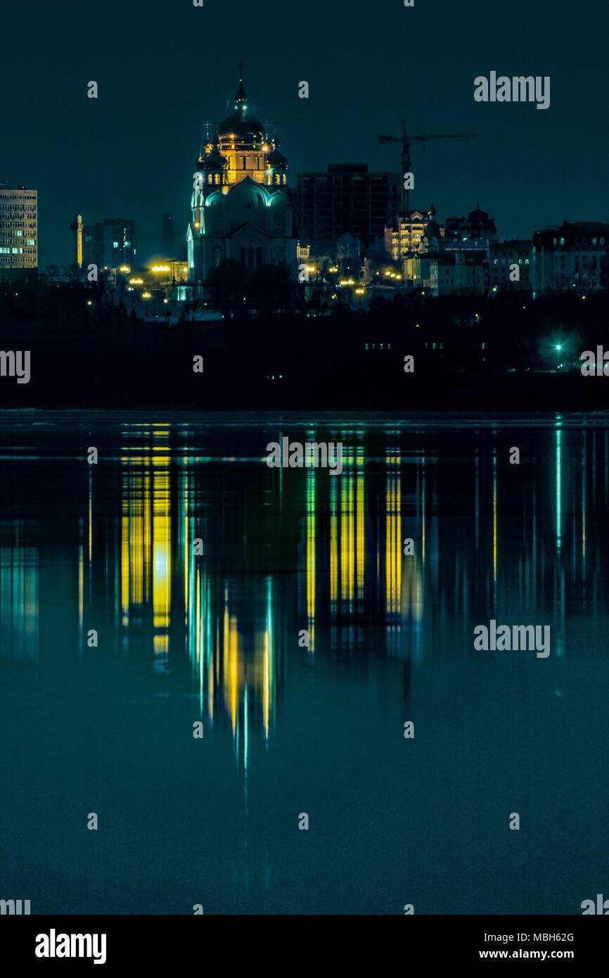 Night city view with lots of lights and its reflection in a river water ...