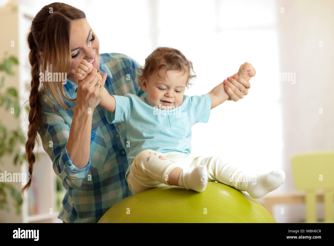 Happy mother and baby boy on fitness ball in nursery at home ...
