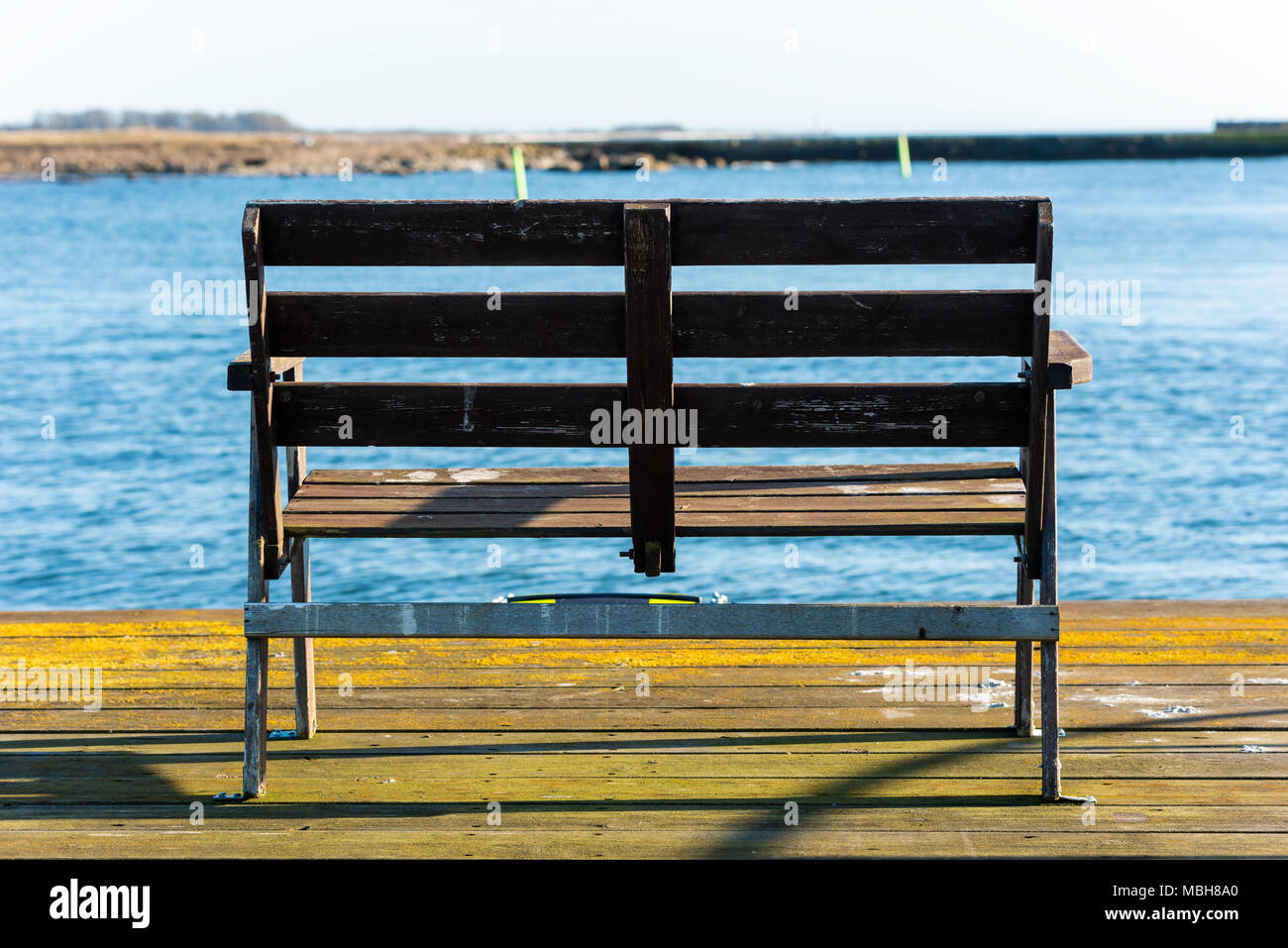 Empty wooden bench at the end of a pier with a blurred view of harbor ...