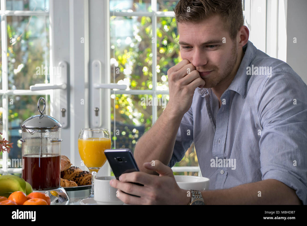 Handsome man sitting at breakfast table with cereal, fruit, flowers ...