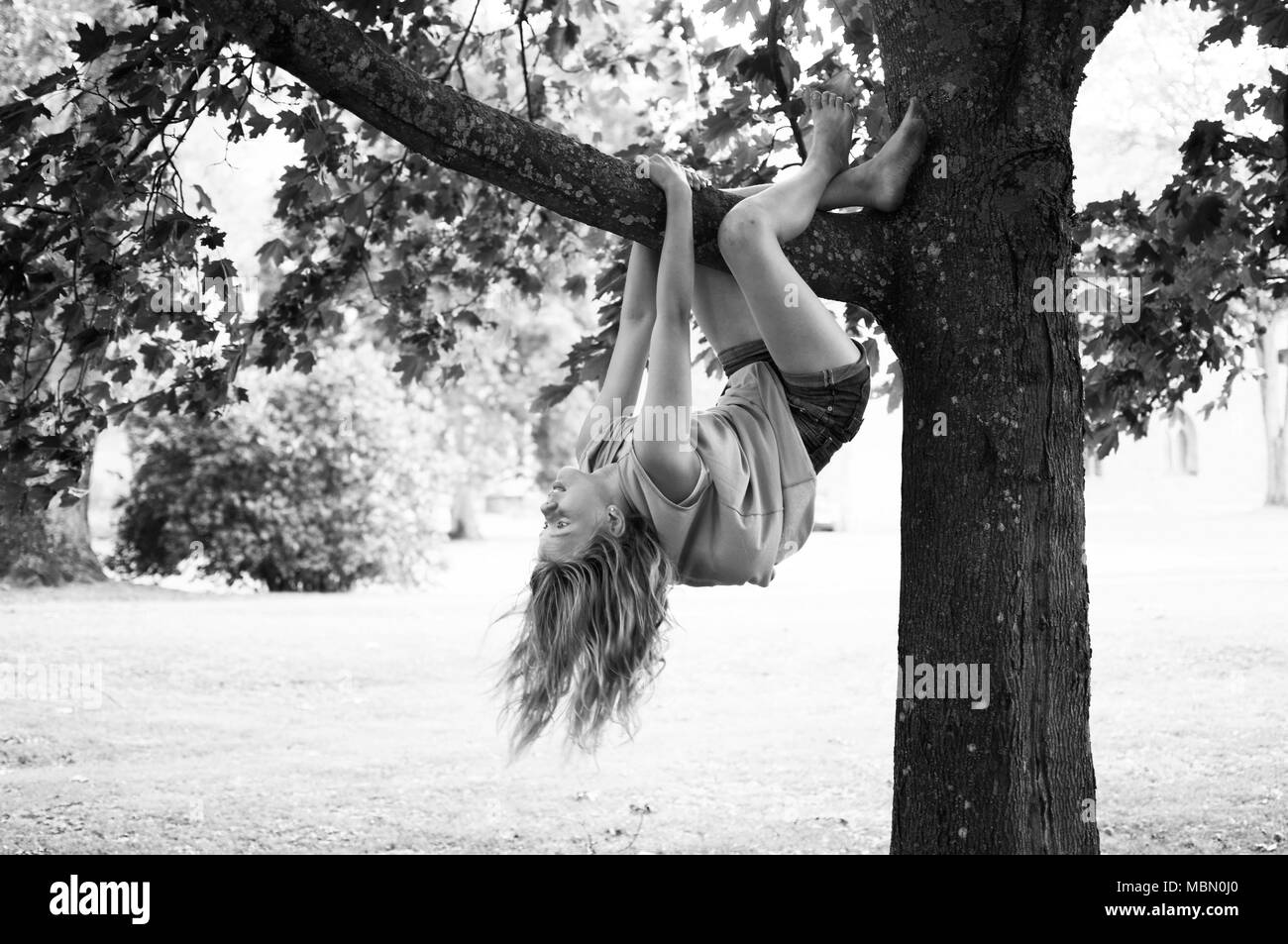 Yong girl with long blond hair hanging from tree in park. Black and ...