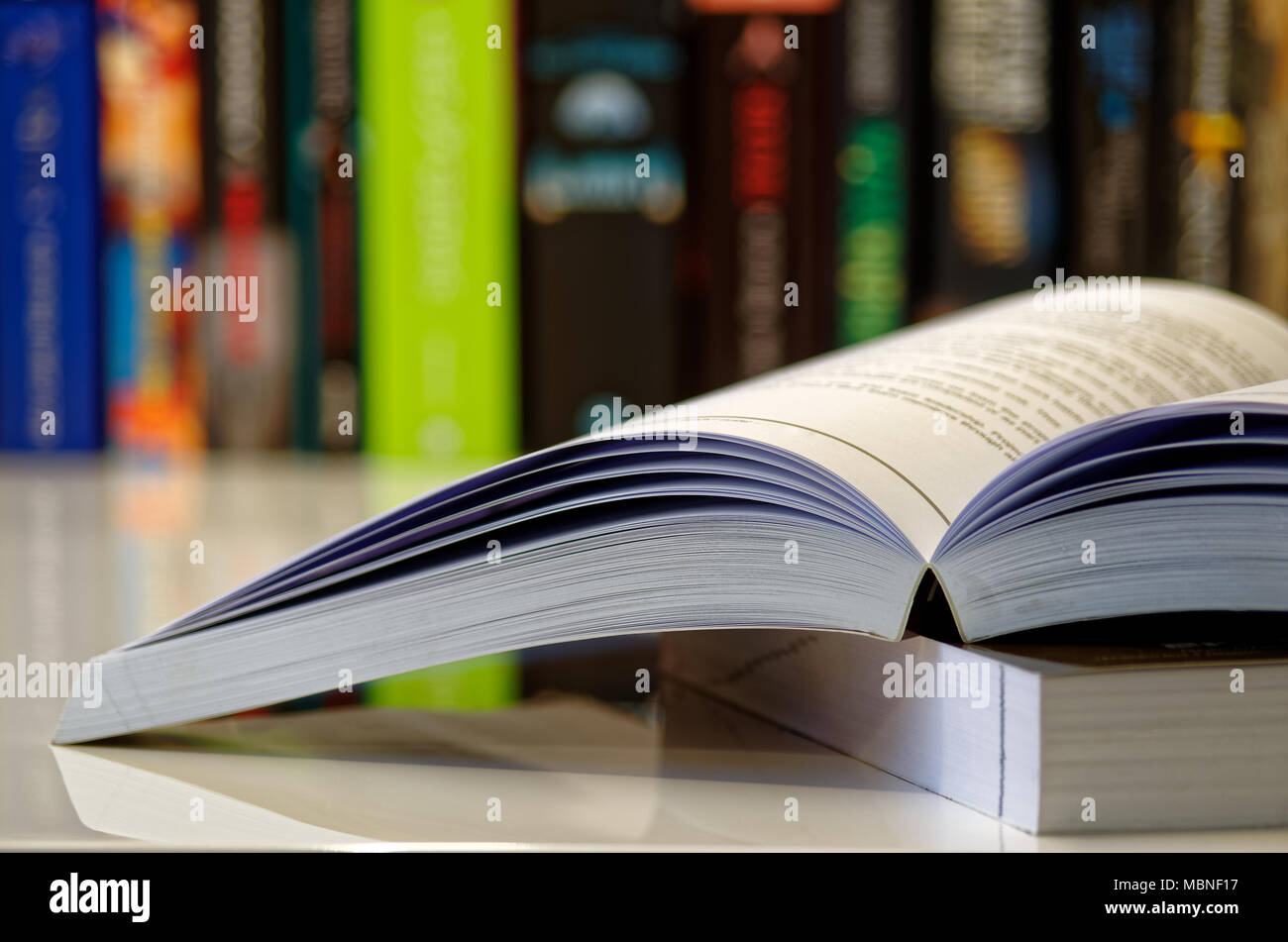 Open book lying on a white table and colorful books in a row in ...