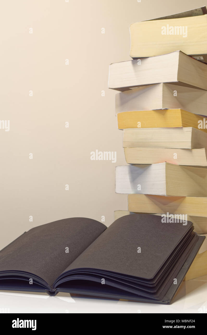 Black open book in foreground of pile of books on the white table and ...