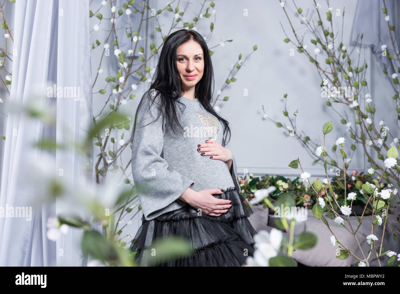 Adorable pregnant brunette woman in a dress keeping hands on belly ...