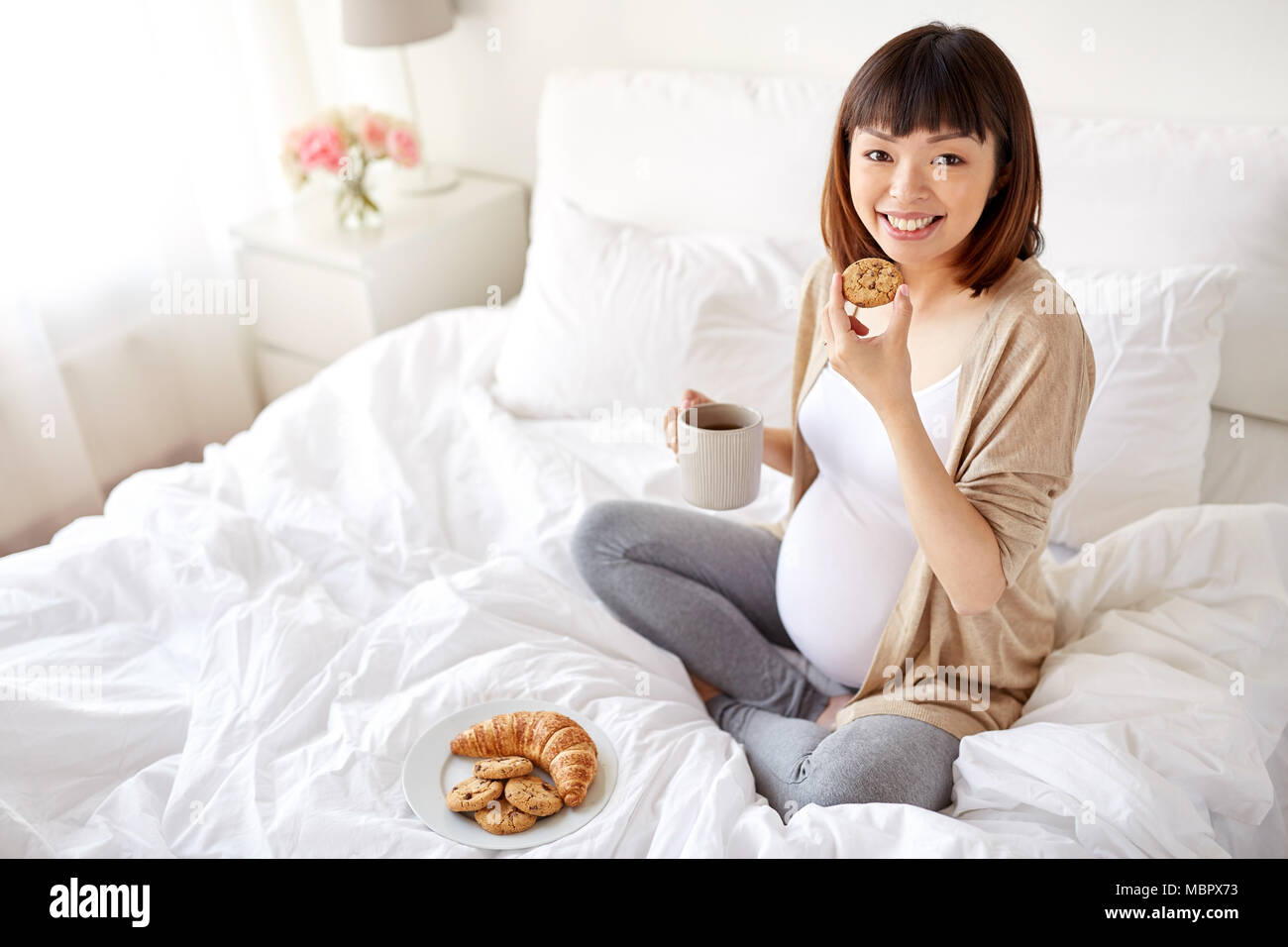 happy pregnant woman eating cookie in bed at home Stock Photo - Alamy
