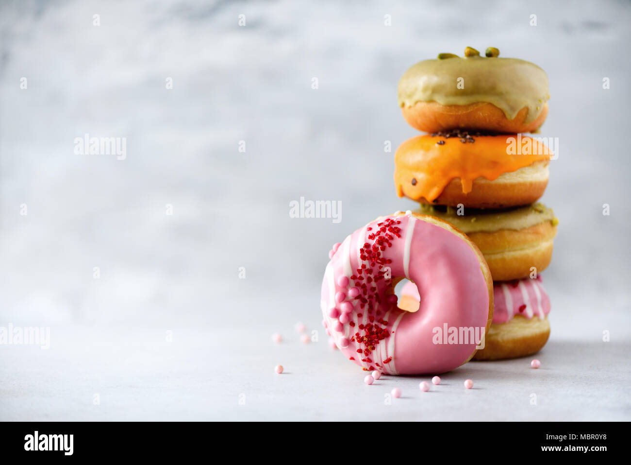 Stack of glazed colorful assorted donuts with sprinkles on grey cement ...