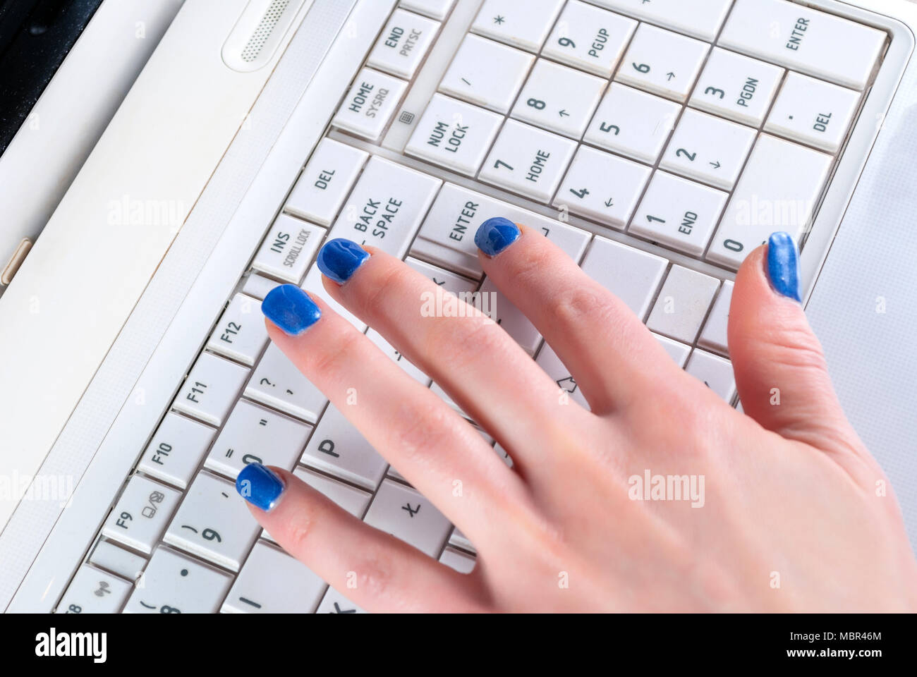 Woman hand with blue nails pressing button on white laptop keyboard ...