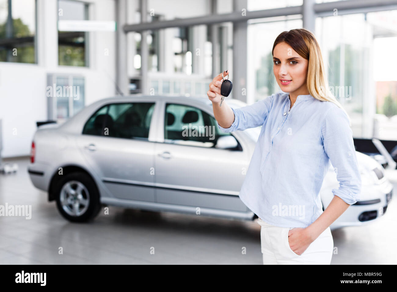 Blonde business woman standing in modern car dealership and holding car ...