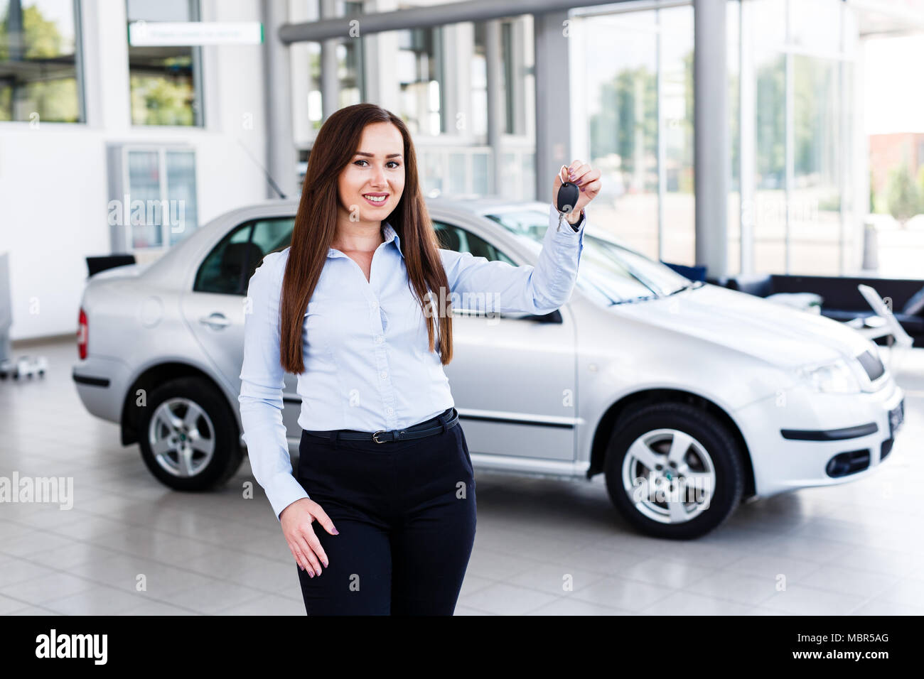 Beautiful business woman standing in modern car dealership and holding ...
