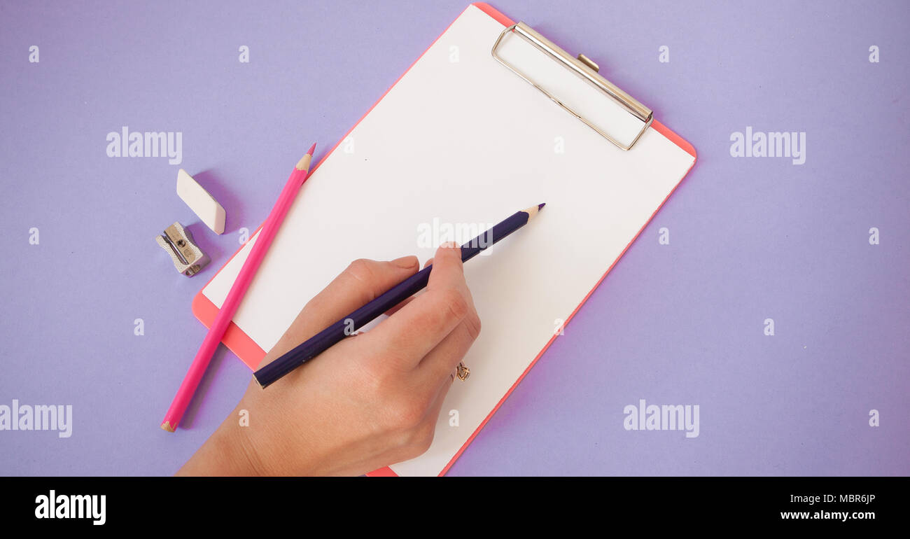 Flatlay with woman's hand holding pencil and notebook on a violet ...