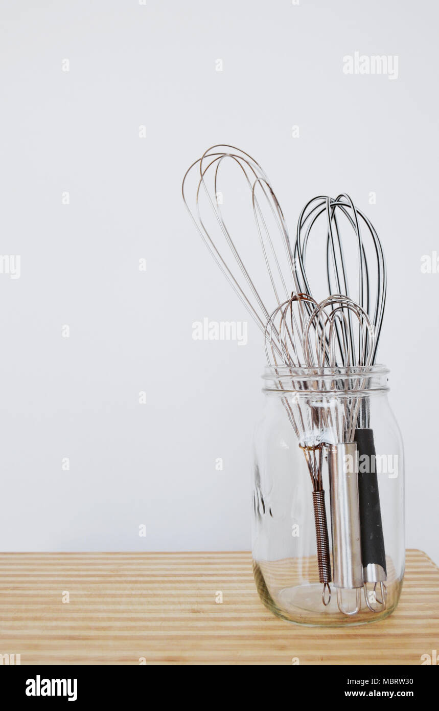 A collection of four whisks of different sizes in a glass jar on a wood ...