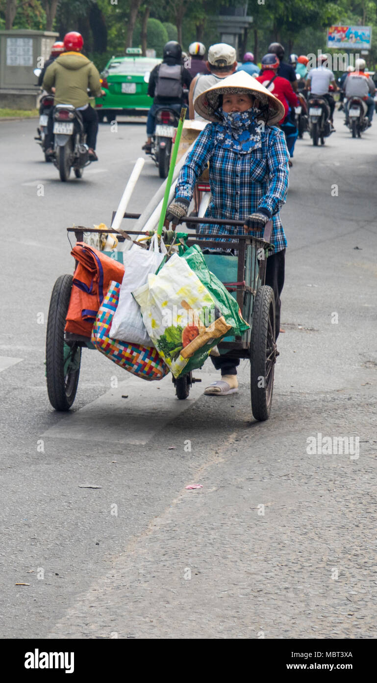 A Vietnamese female worker wearing a traditional conical hat, pushing a ...