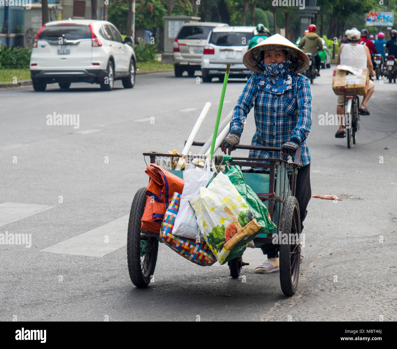 A Vietnamese female worker wearing a traditional conical hat, pushing a ...