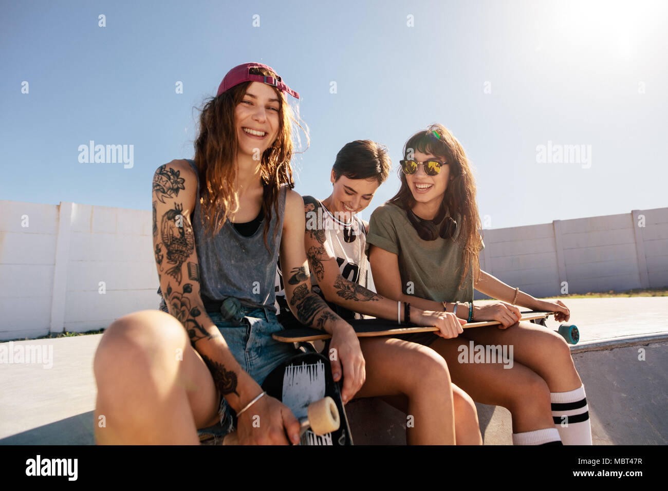 Beautiful woman sitting on ramp with friends at skate park. Cheerful ...