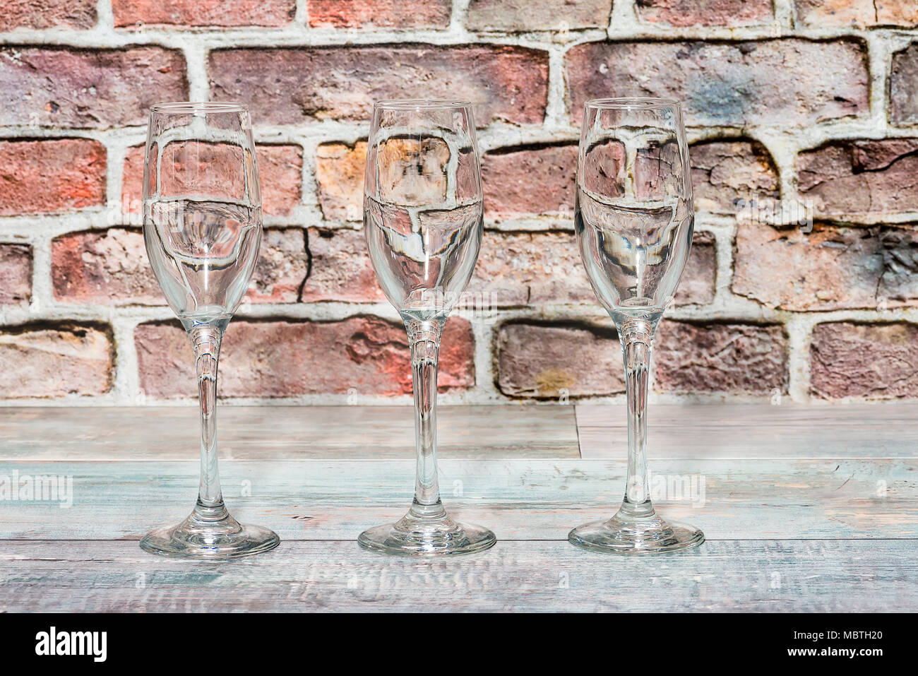 three empty glass goblets on a rustic wooden board and with red bricks ...