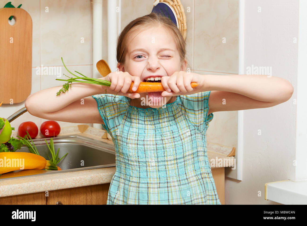 girl posing in home kitchen with fresh fruits and vegetables, eating a ...