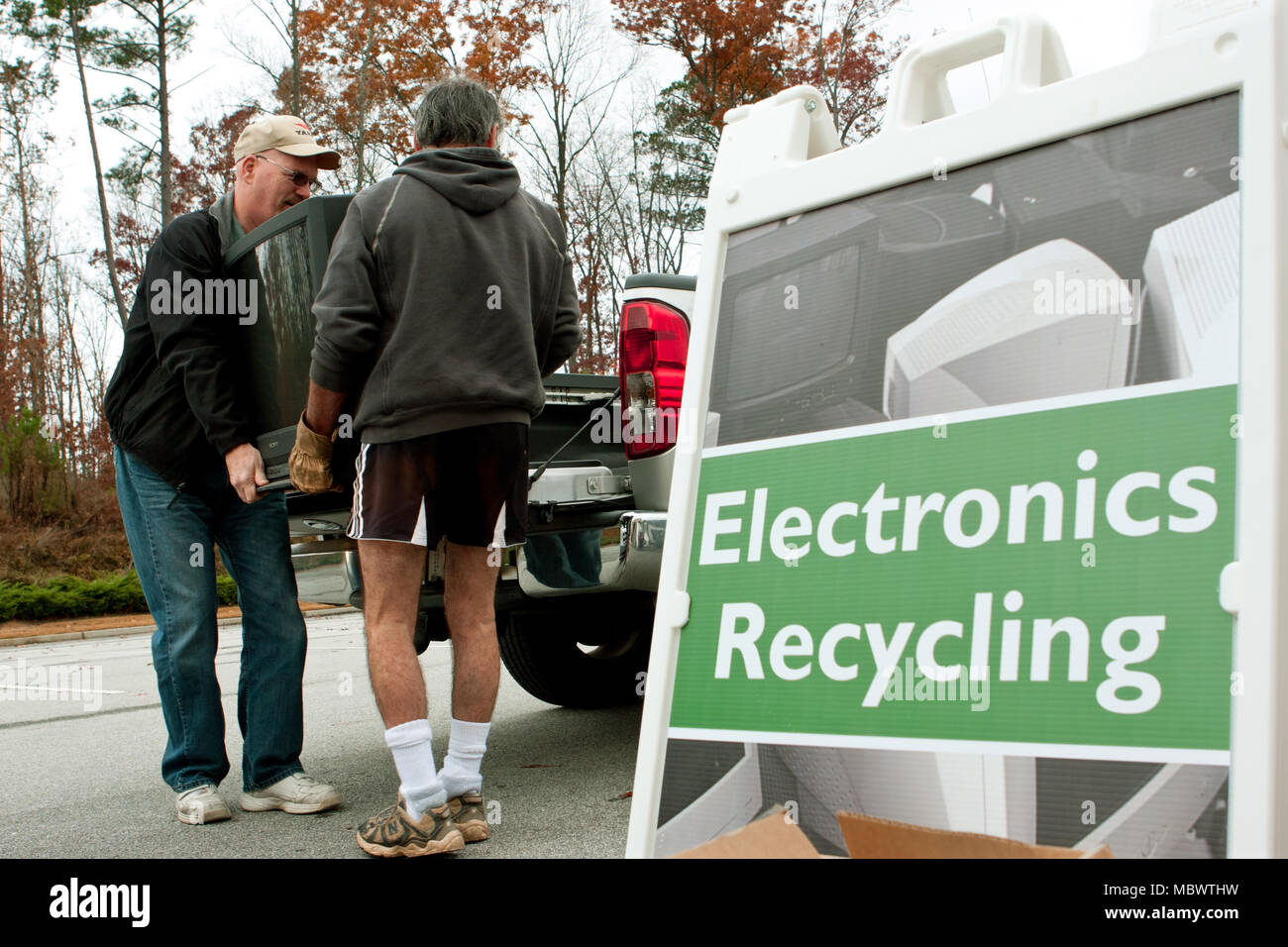 Two men carry a discarded television set past an "Electronics Recycling ...