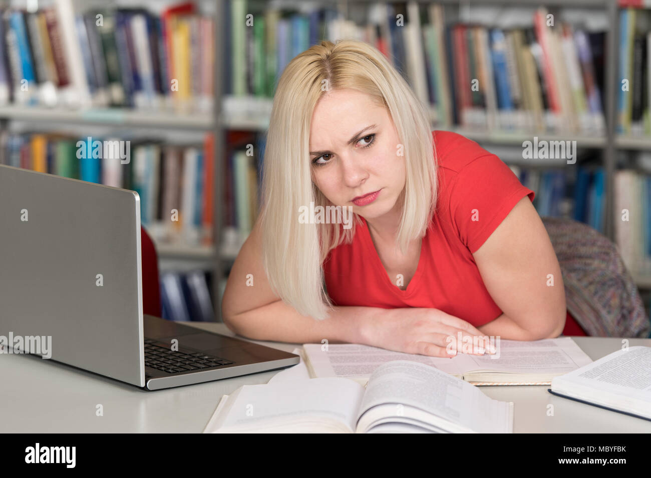 Stressed Young Female Student Reading Textbook While Sitting in Library ...