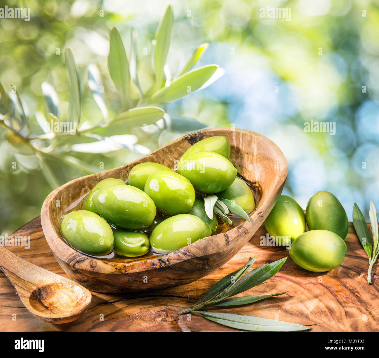 Whole table olives in the wooden bowl on the table. Nature background ...