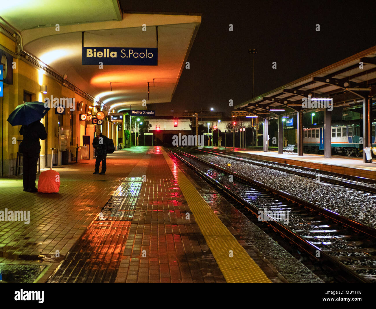 Two train drivers in station on a rainy night. Wet rails in the rain in ...