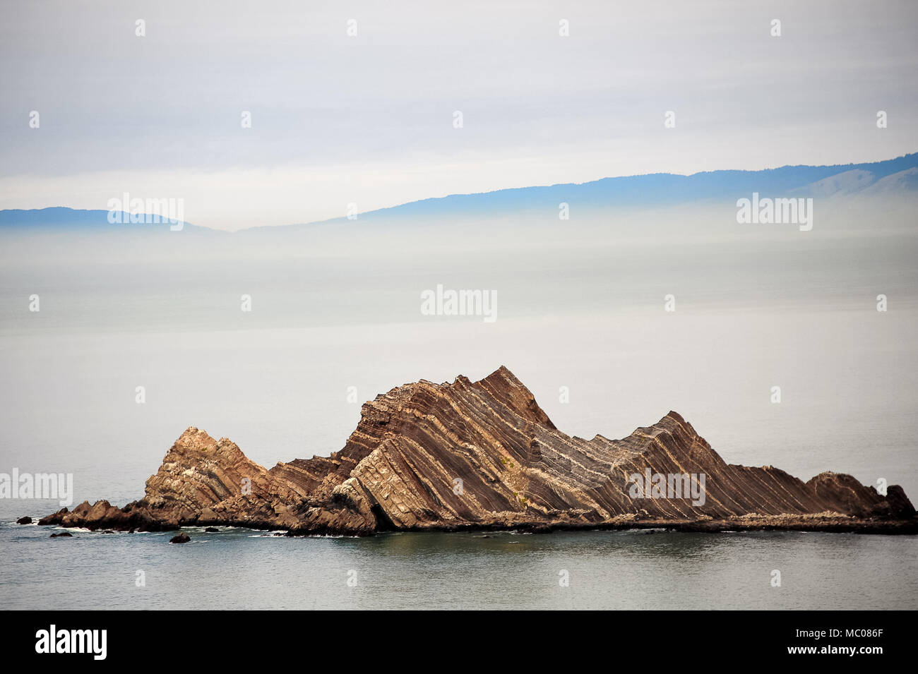 Multi-coloured layers of a sedimentary rock, rise out of the ocean in a ...