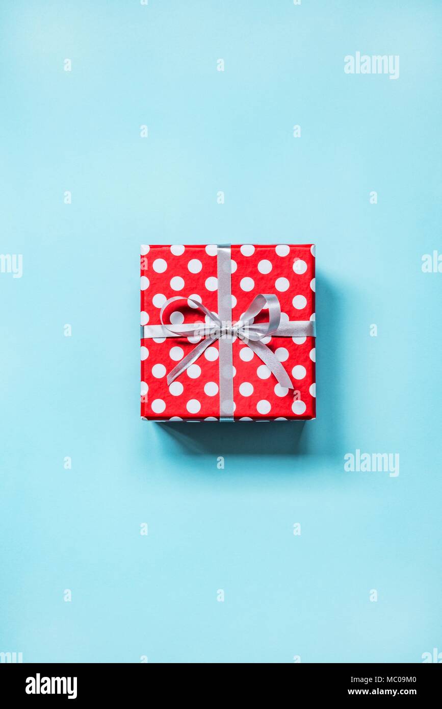 Top view of a red dotted gift box tied with golden bow over blue ...