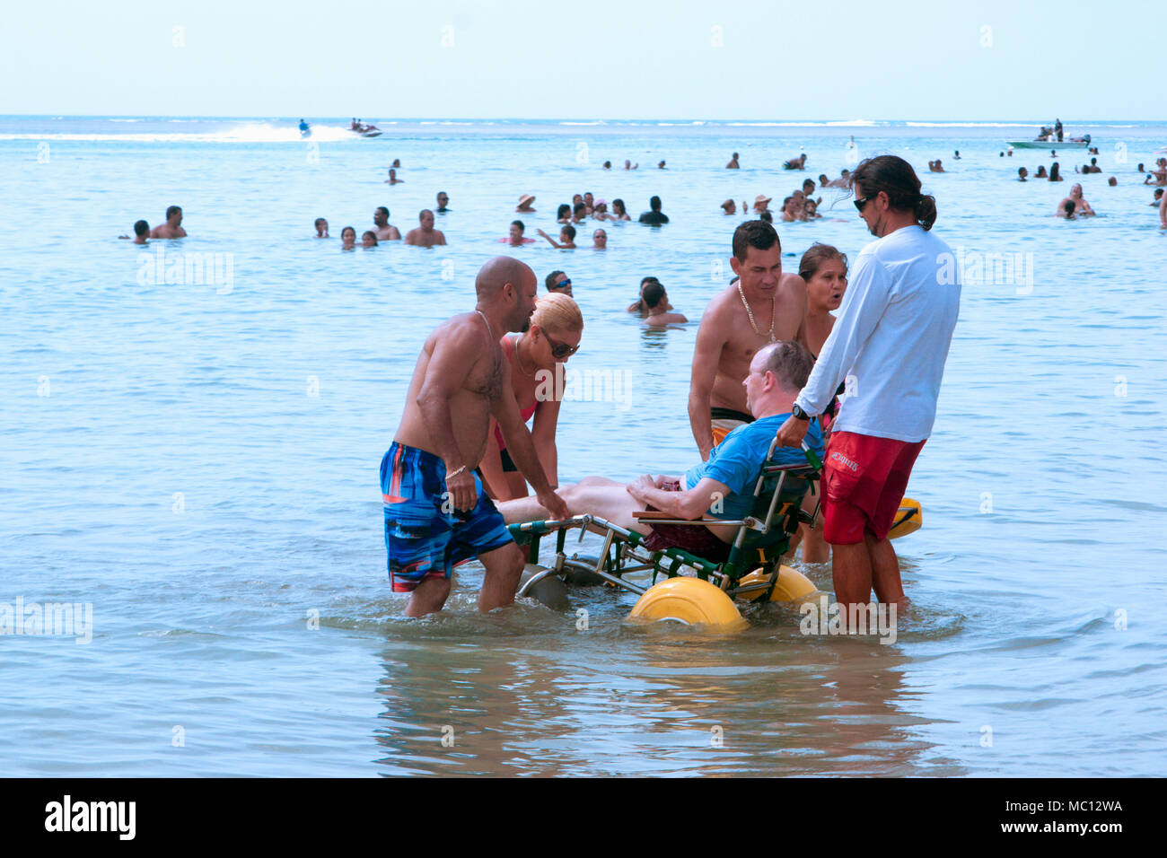 Staff assist man in water based wheelchair in the ocean, Luqillo Beach ...