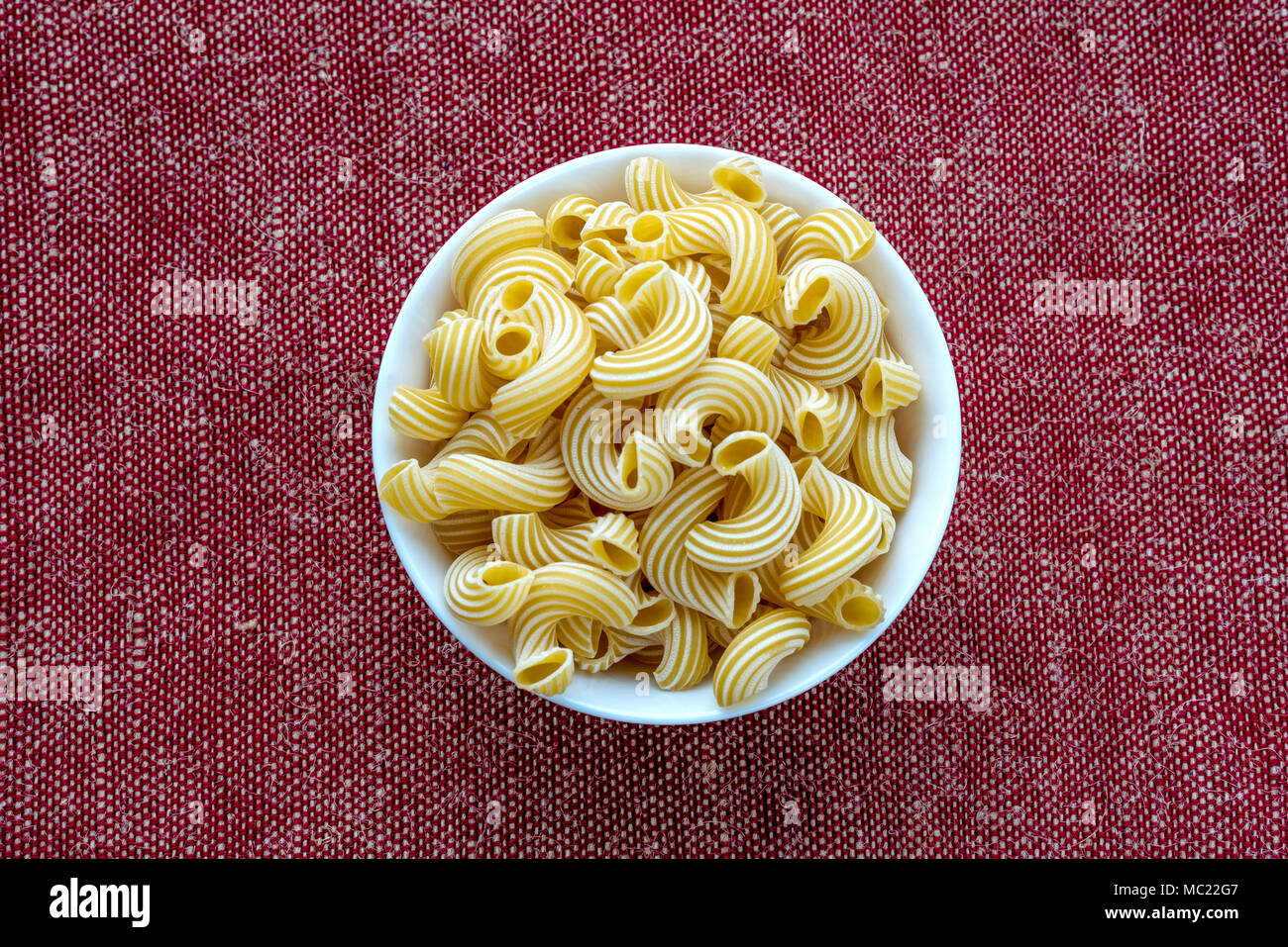 rigati pasta in a white bowl on a red brown cloth burlap background in ...