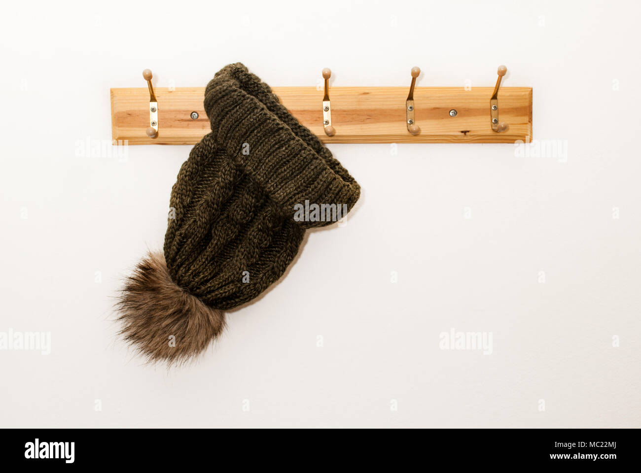 Winter wool cap with a furry ball hanging on a hat stand on white ...