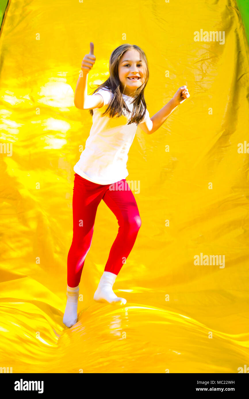 Happy little girl showing thumb up after sliding on a inflatable castle ...