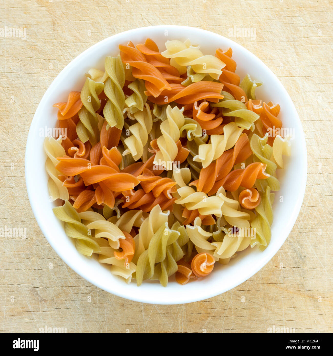 Multicolor spiral macaroni pasta in a white cup on a wooden table ...