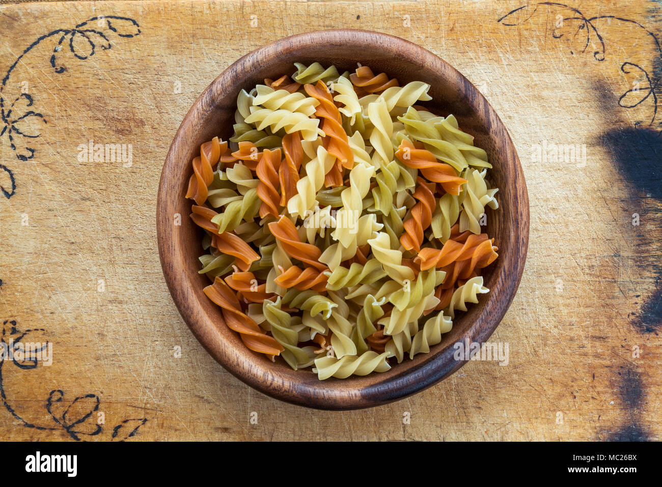 Multicolor spiral macaroni pasta in a wooden bowl on a cutting wooden ...