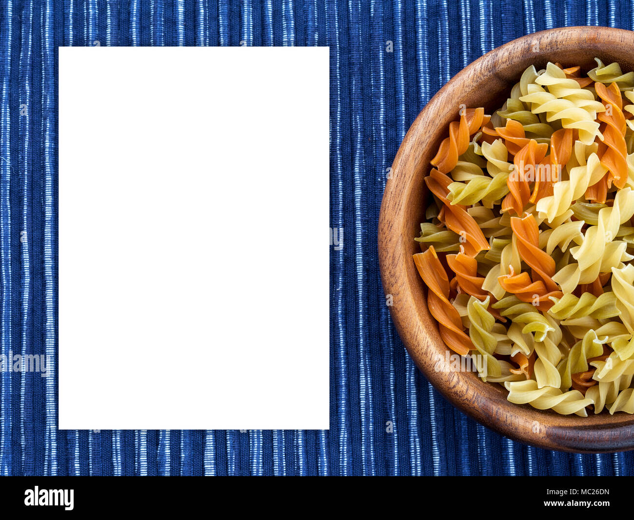 Multicolor spiral macaroni pasta in a wooden bowl on a striped white ...