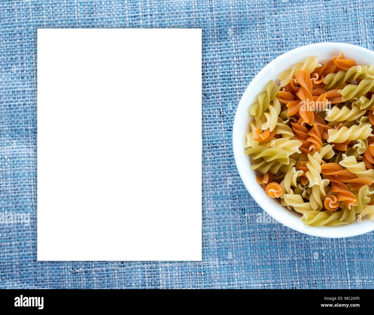 Multicolor spiral macaroni pasta in a white bowl on a blue knitted ...