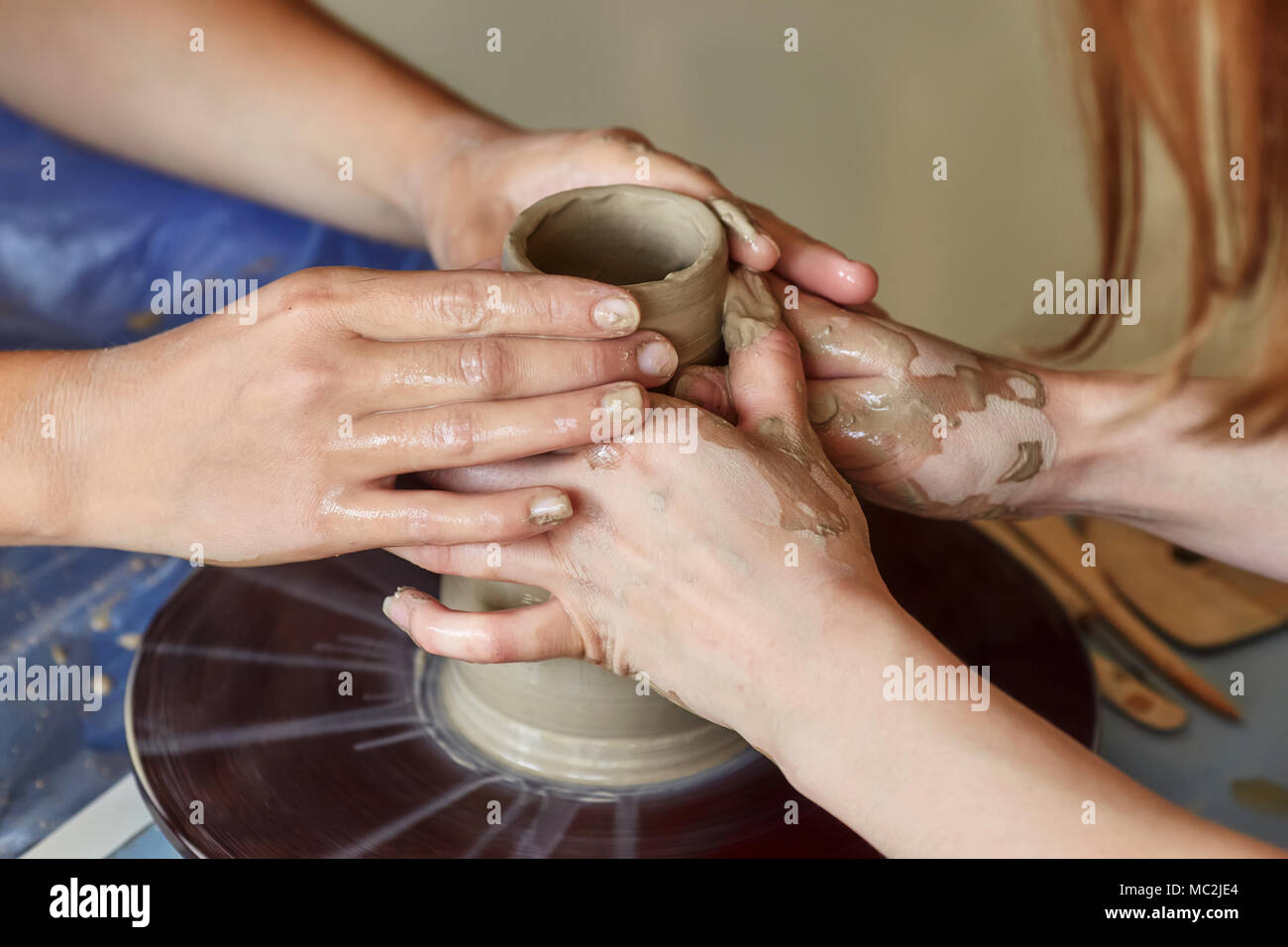 Hands of two people create pot on potter's wheel. Teaching pottery ...