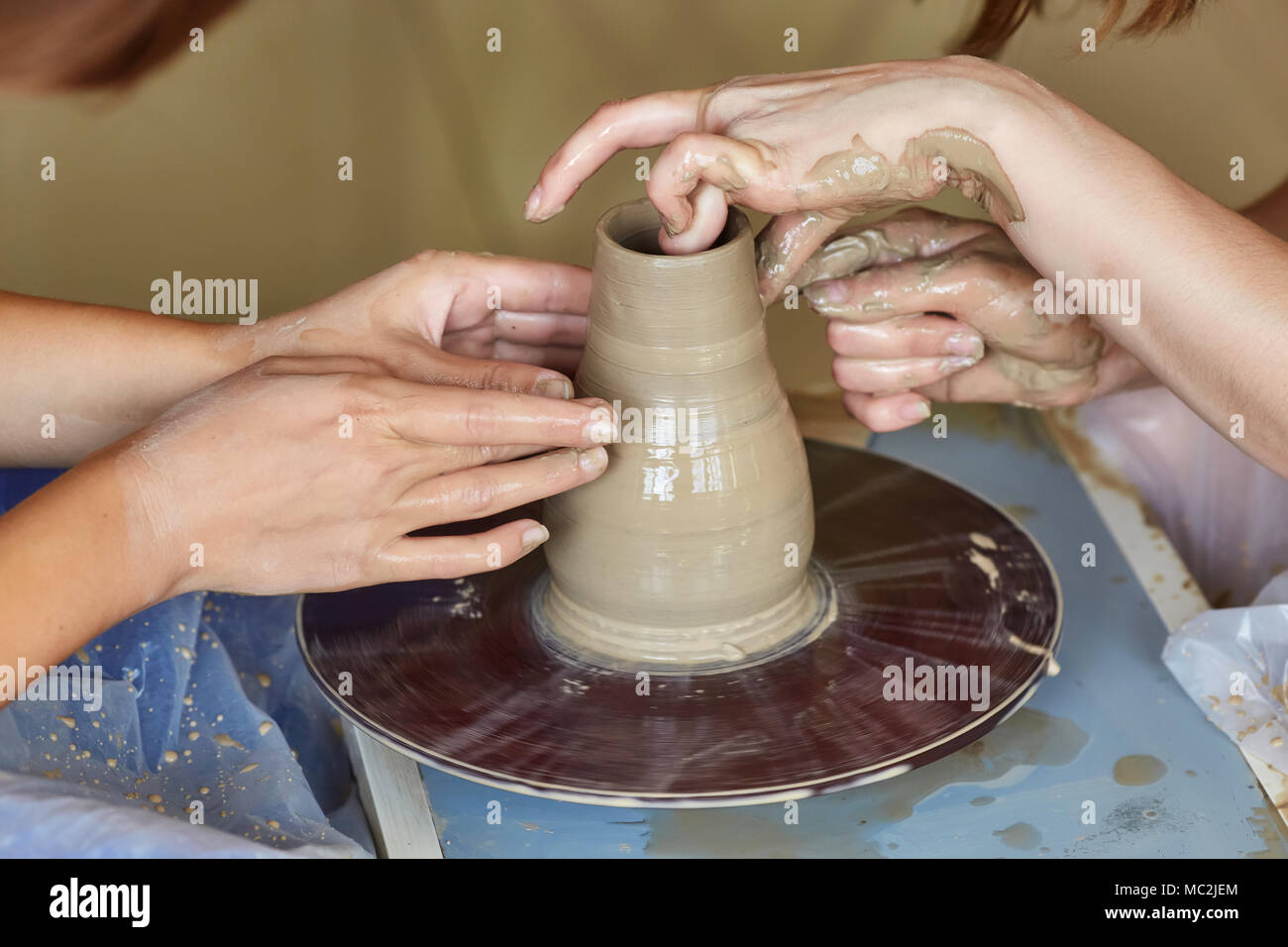 Hands of two people create pot on potter's wheel. Teaching pottery ...