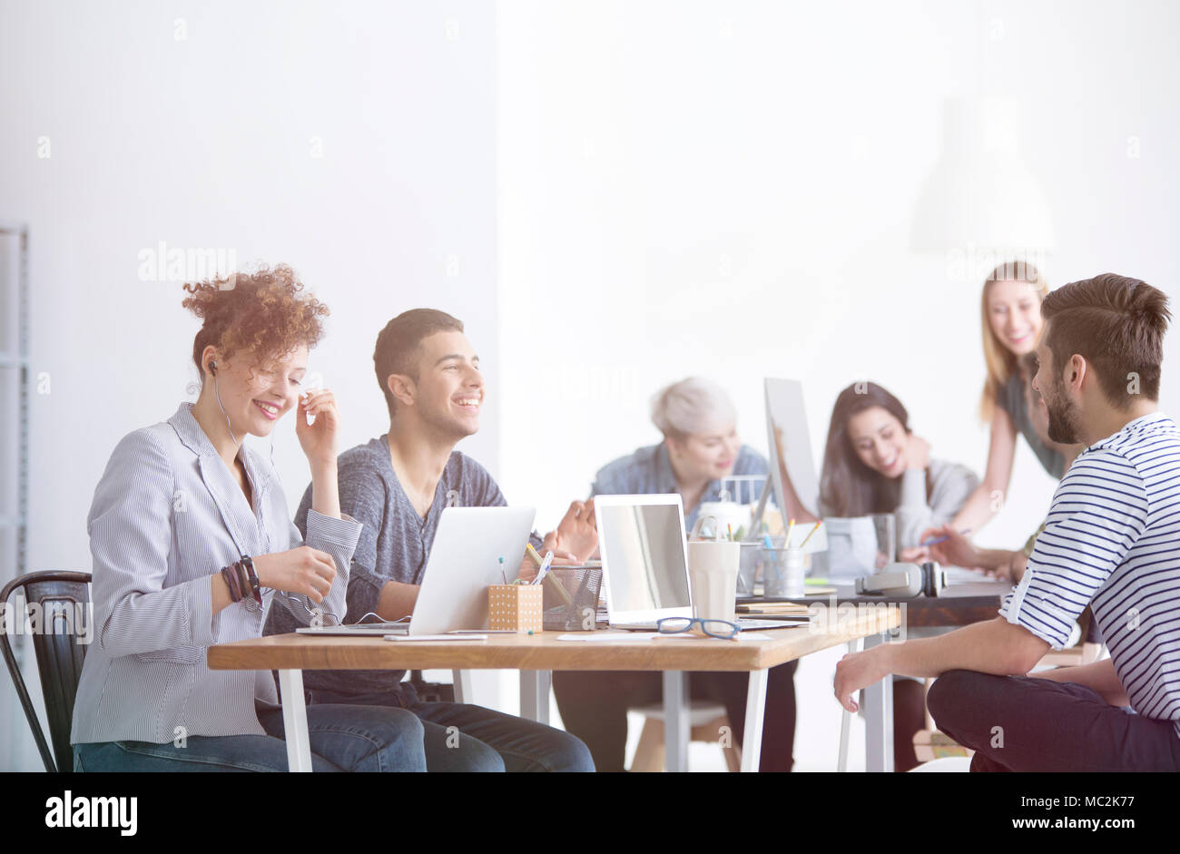 A group of coworkers smiling and talking while working on their laptops ...