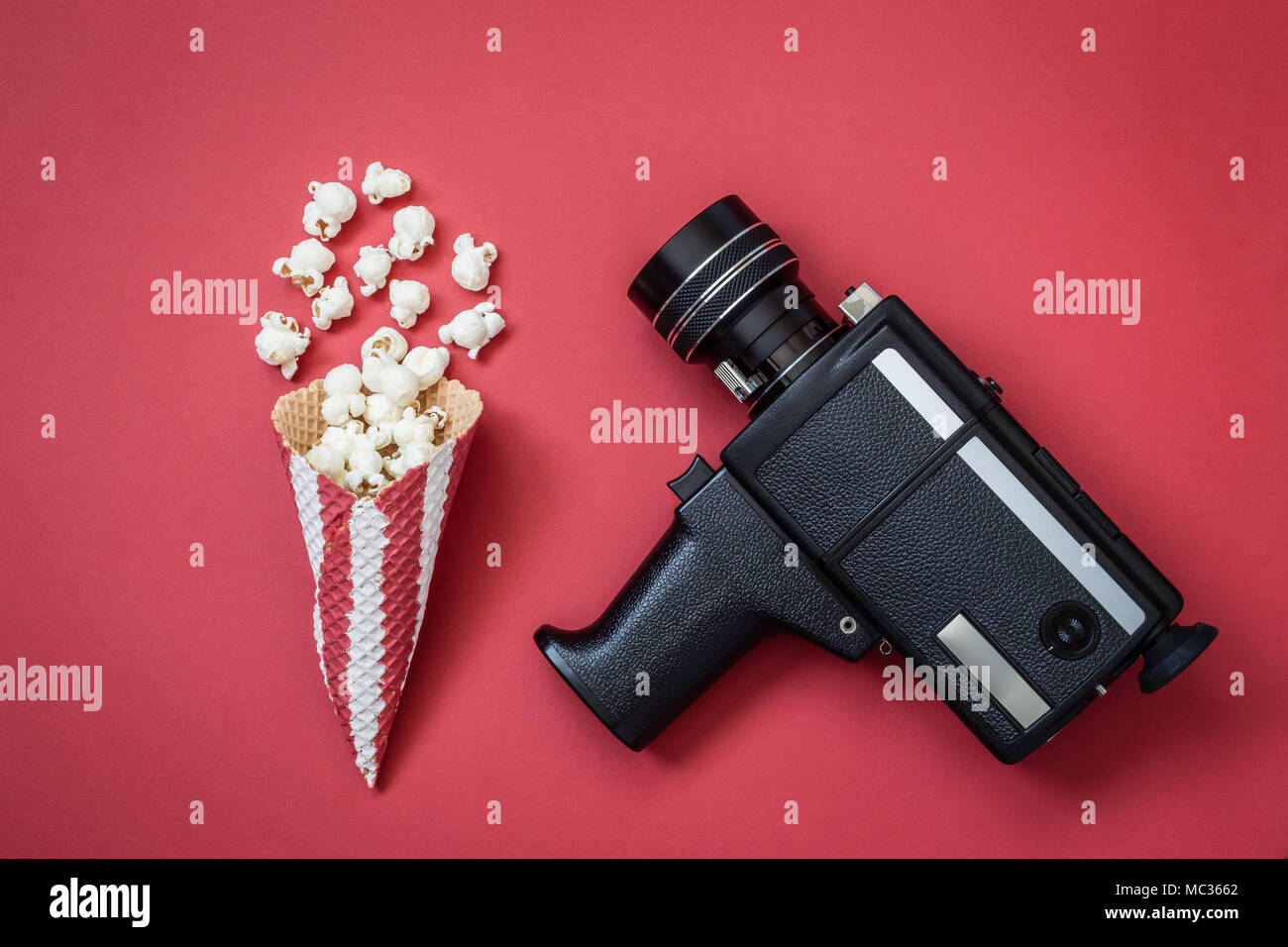 Flat lay of cone with popcorn and retro camcorder on red background ...