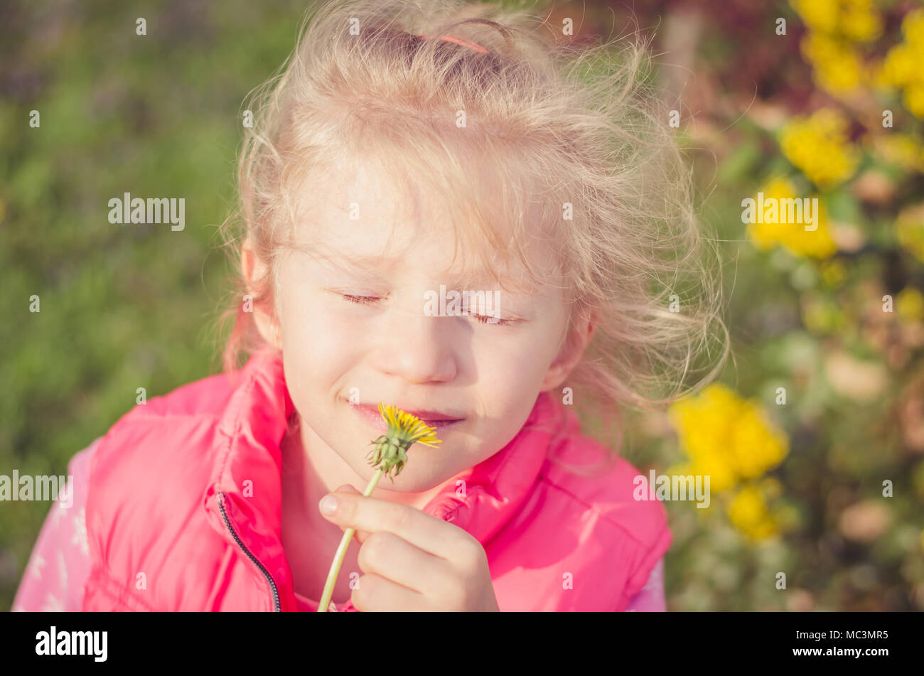 adorable blond girl smelling to flower in spring nature Stock Photo - Alamy