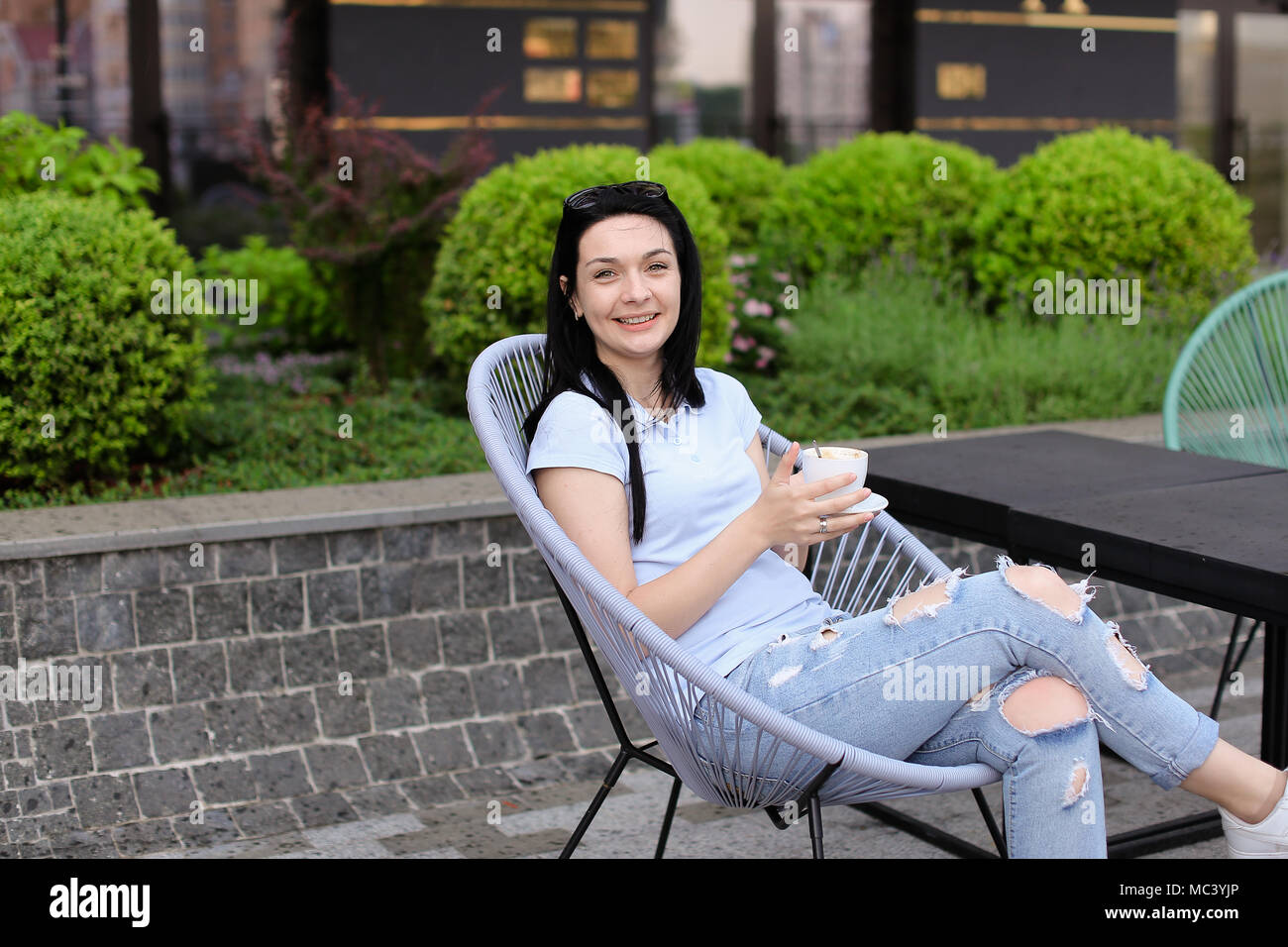 Lady sitting in chair at cafe near green plants and drinking coffee ...